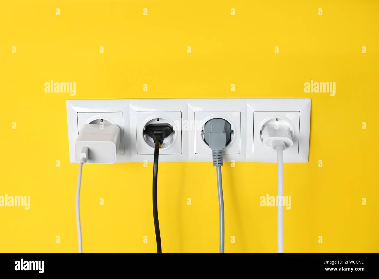 Power sockets with inserted plugs on yellow wall. Electrical supply ...