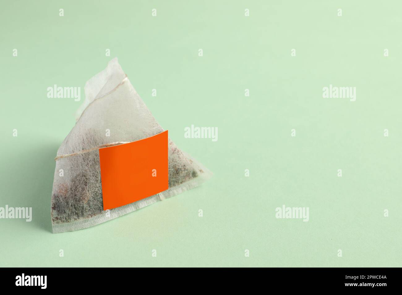 New tea bag with tab on light green background, closeup. Space for text ...