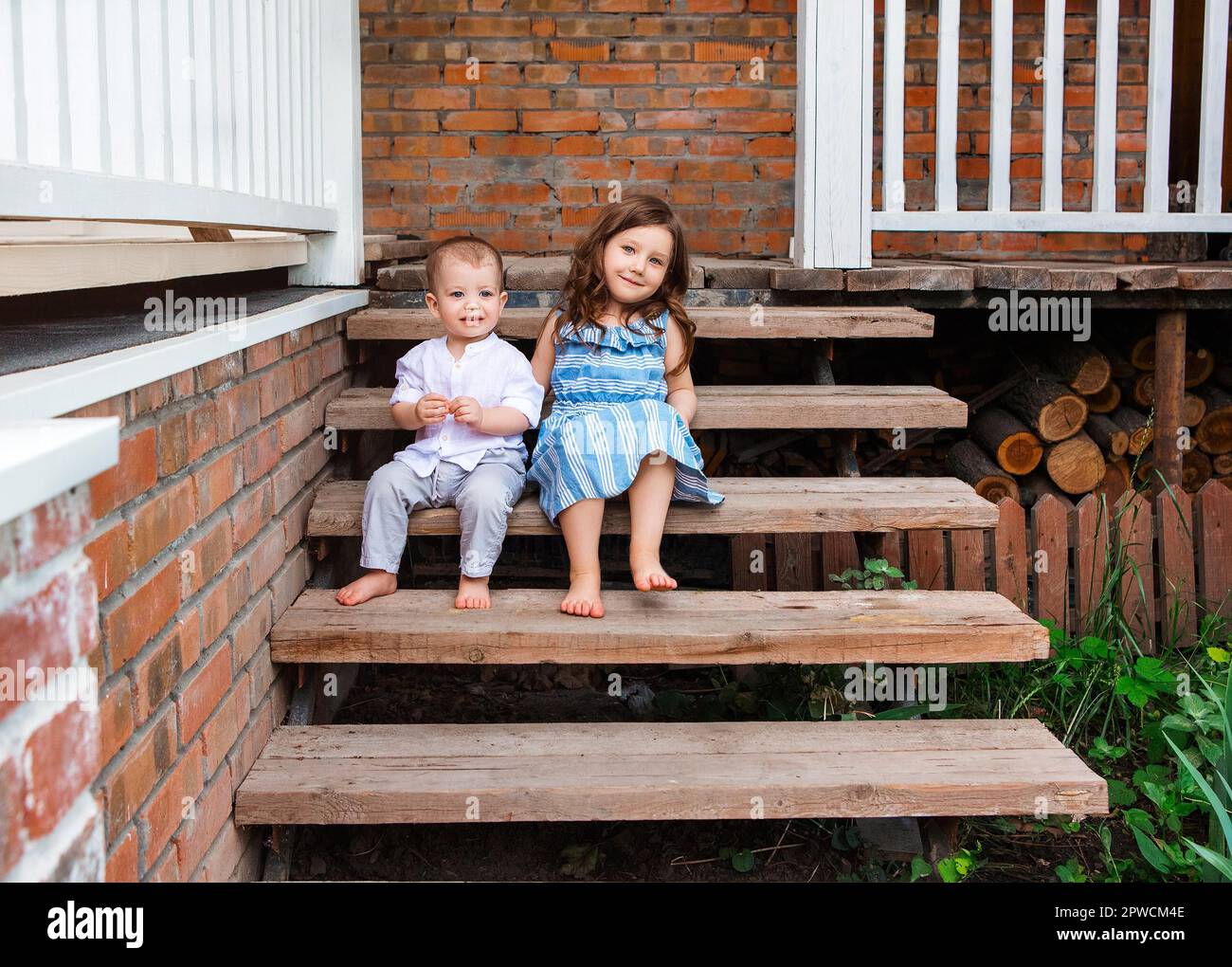 Cute little brother and sister sitting on wooden staircase near porch ...