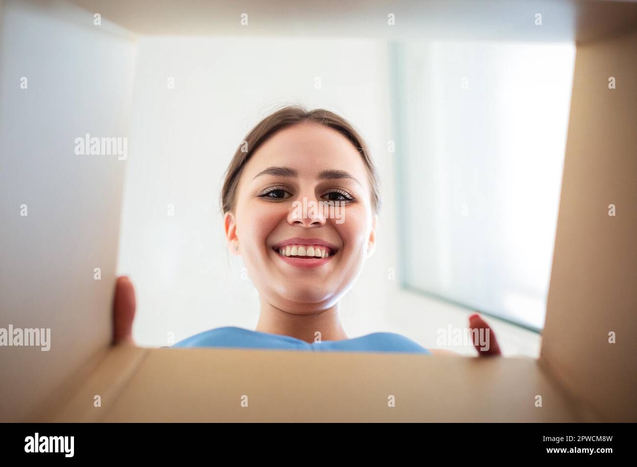 From below happy young female smiling and looking inside carton box ...