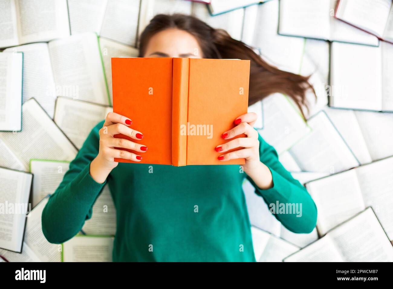 Top view of anonymous female student lying on books and reading during ...