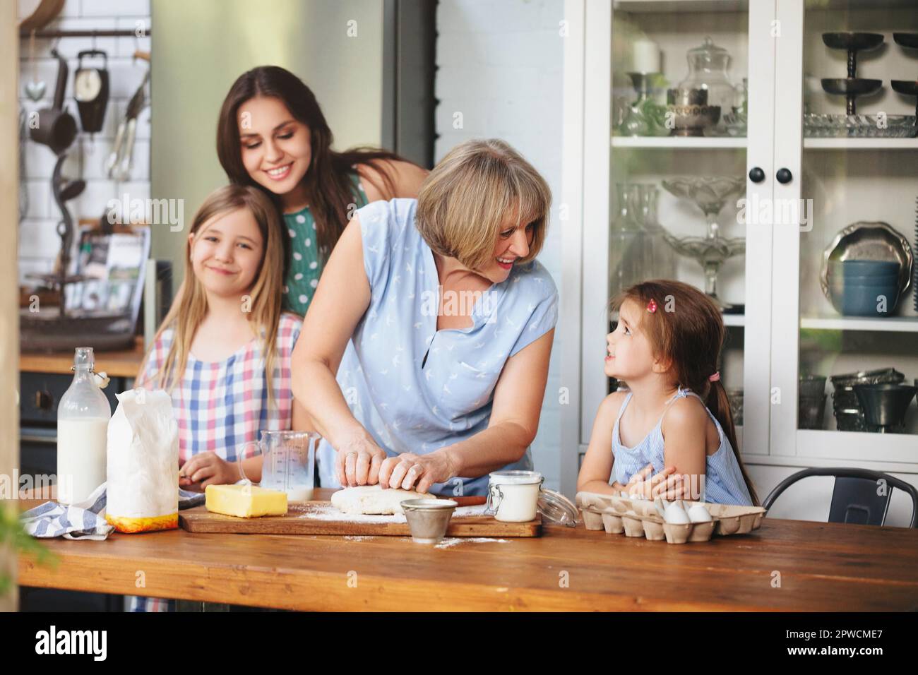 Happy adult and mature women cooking together with cute girls at table ...