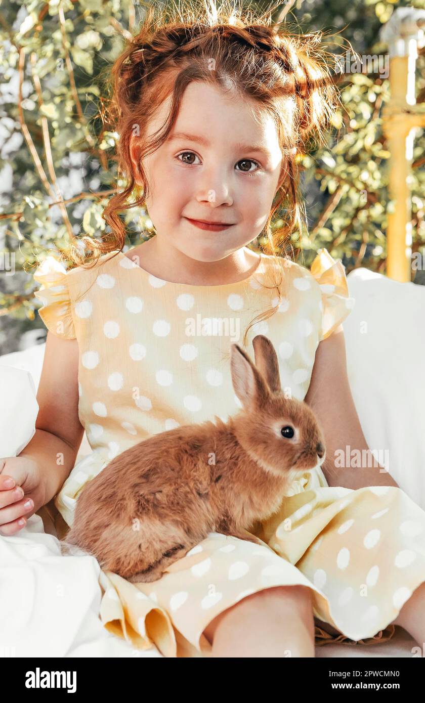 Little pretty girl in summer dress sitting outside on the bed with ...