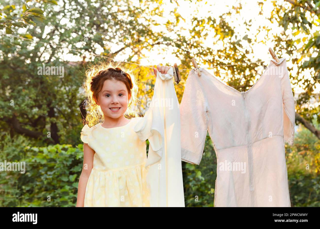 Cute little girl in dress washing white clothes in metal basin in ...