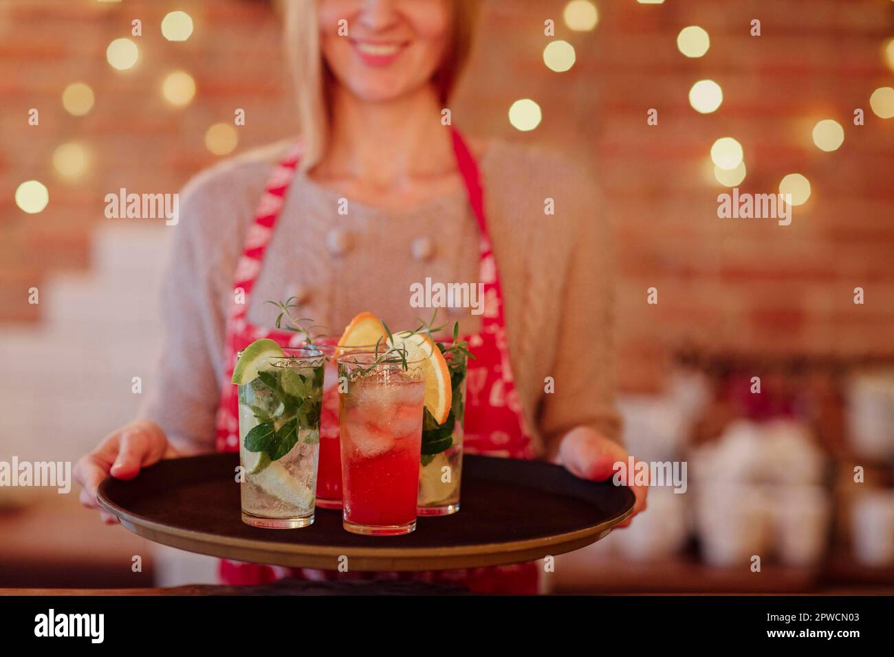 Smiling waitress in colored apron holding tray with alcoholic drinks ...