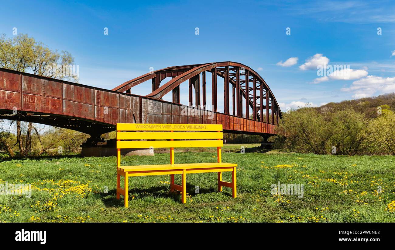 Oversized yellow wooden bench in front of old railway bridge ...
