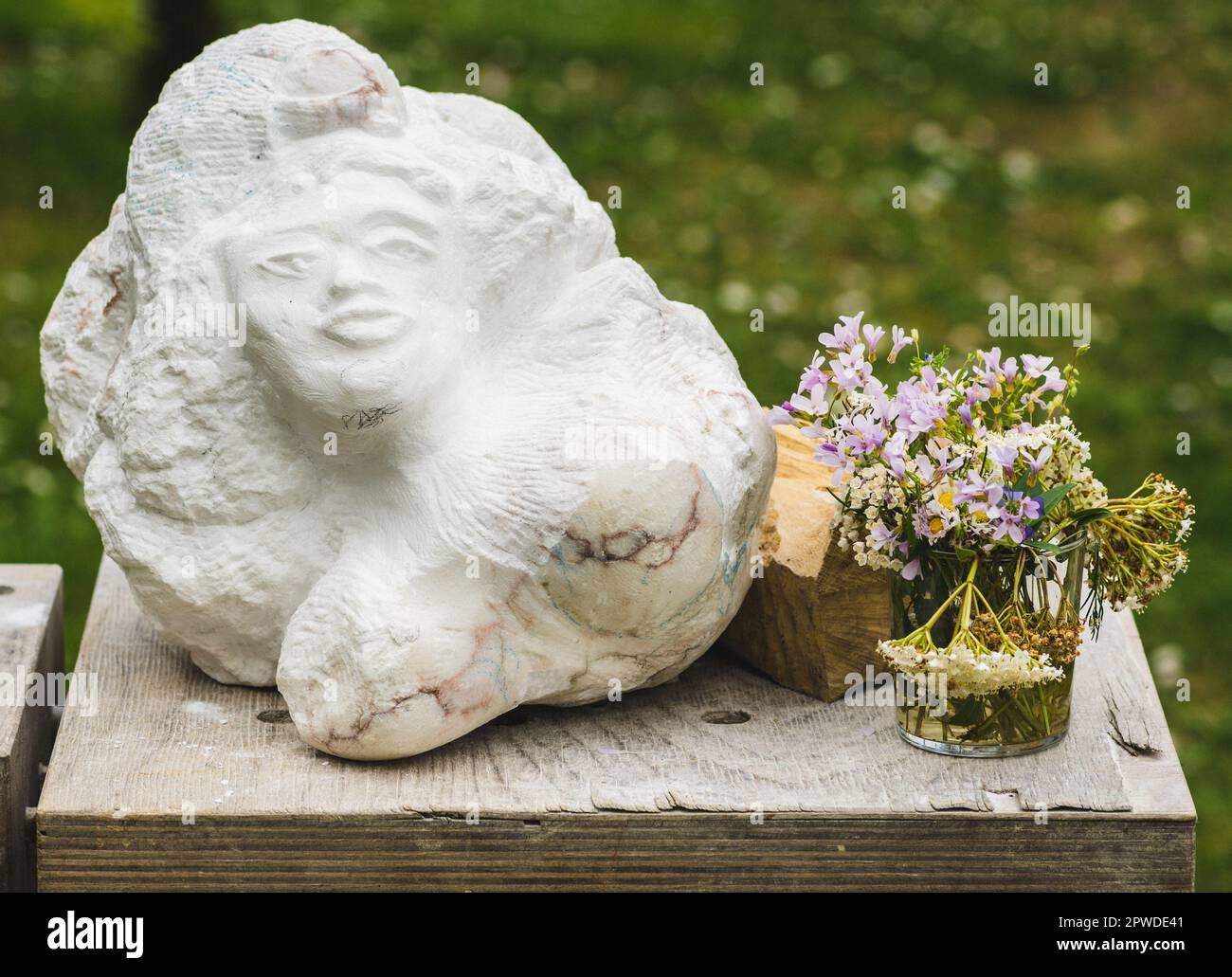 Easel with stone sculpture depicting a female face and spring flowers ...