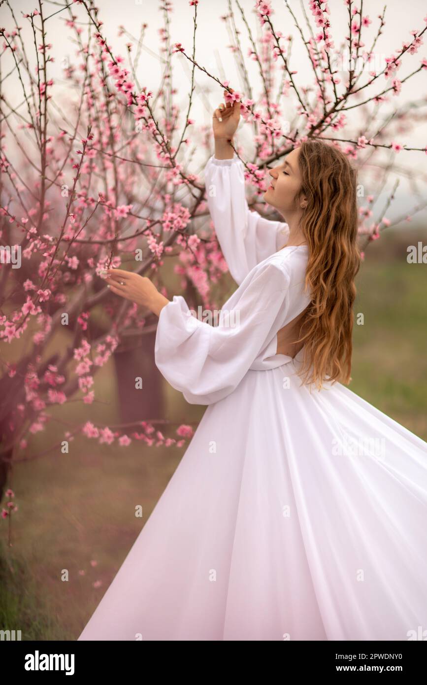 Woman peach blossom. Happy curly woman in white dress walking in the ...