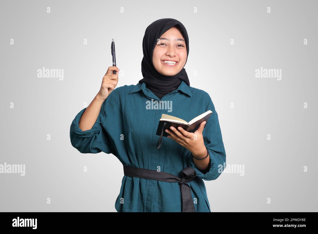 Portrait of excited Asian muslim woman with hijab writing on note book ...