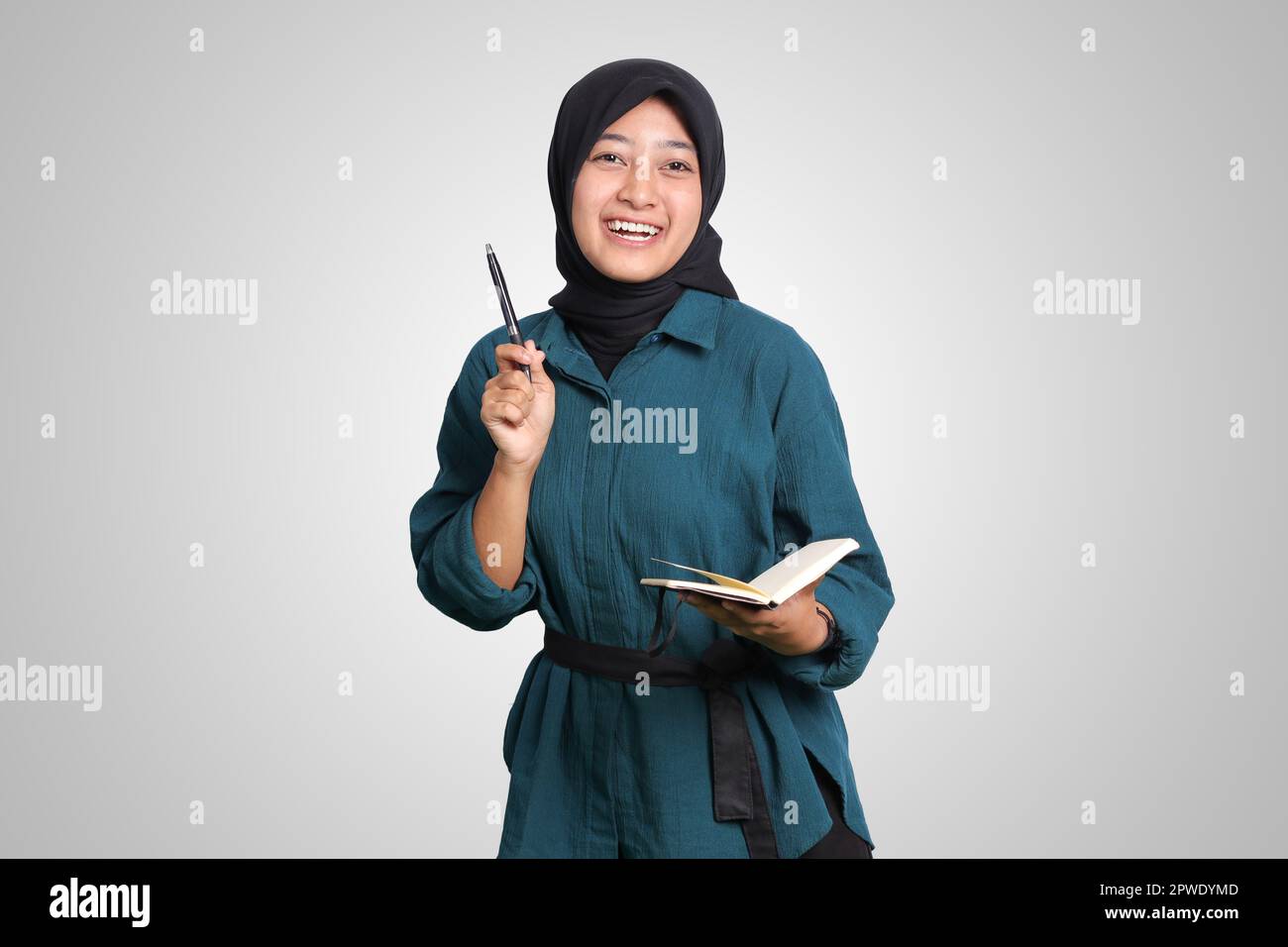 Portrait of excited Asian muslim woman with hijab writing on note book ...