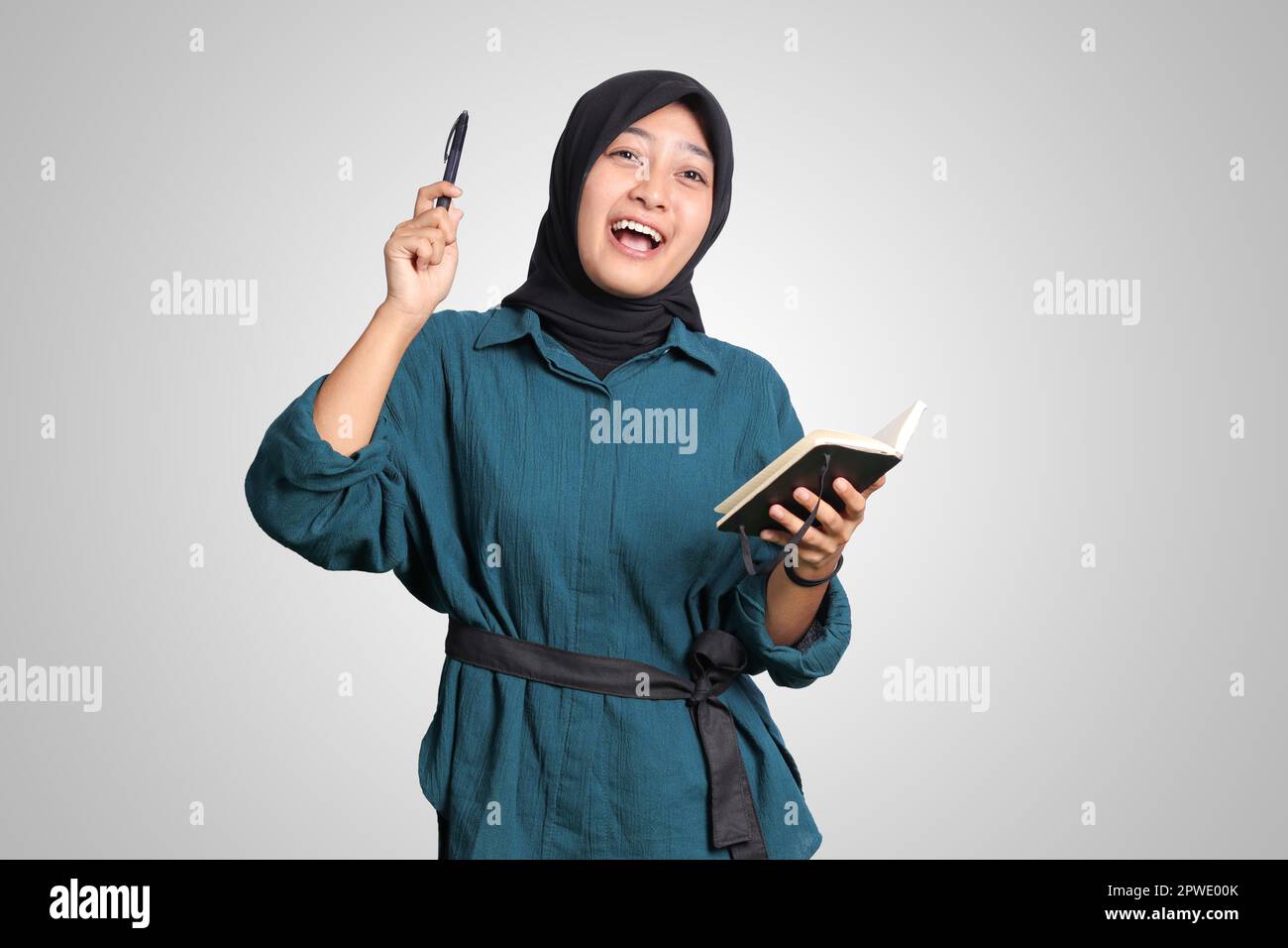 Portrait of excited Asian muslim woman with hijab writing on note book ...