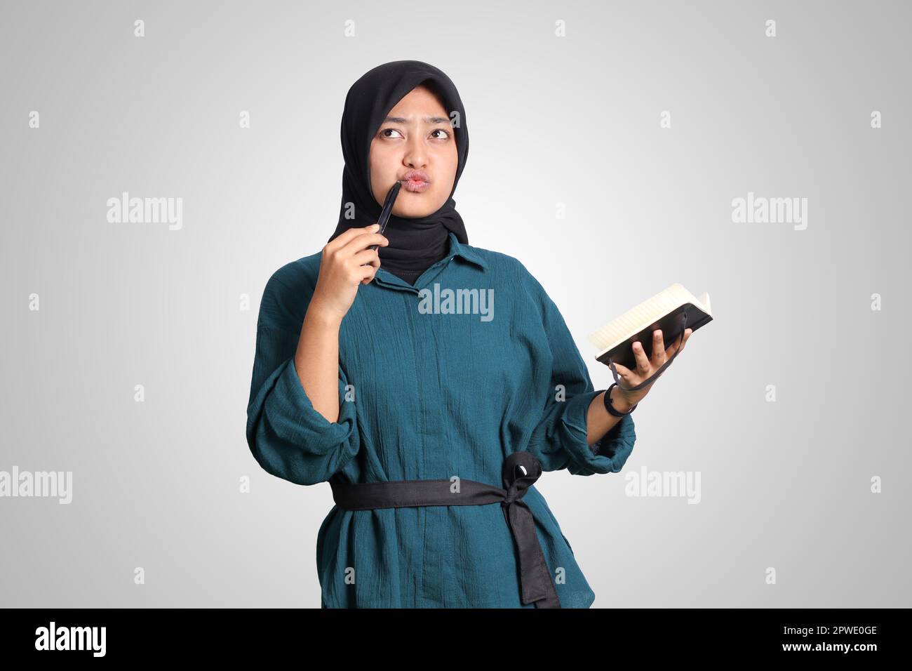 Portrait of excited Asian muslim woman with hijab writing on note book ...