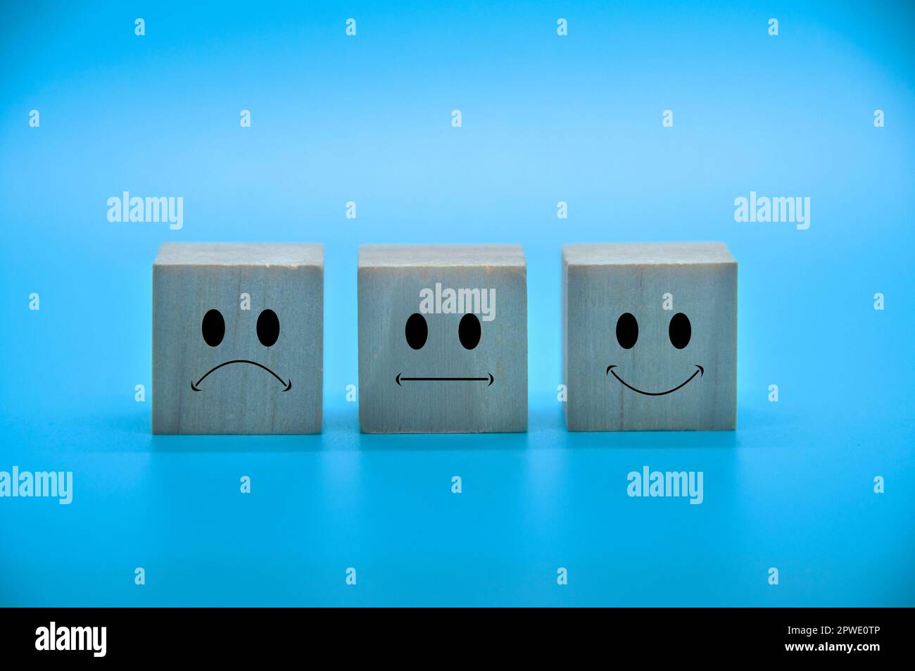 Sad, neutral and happy emoticon faces on wooden cubes with blue ...