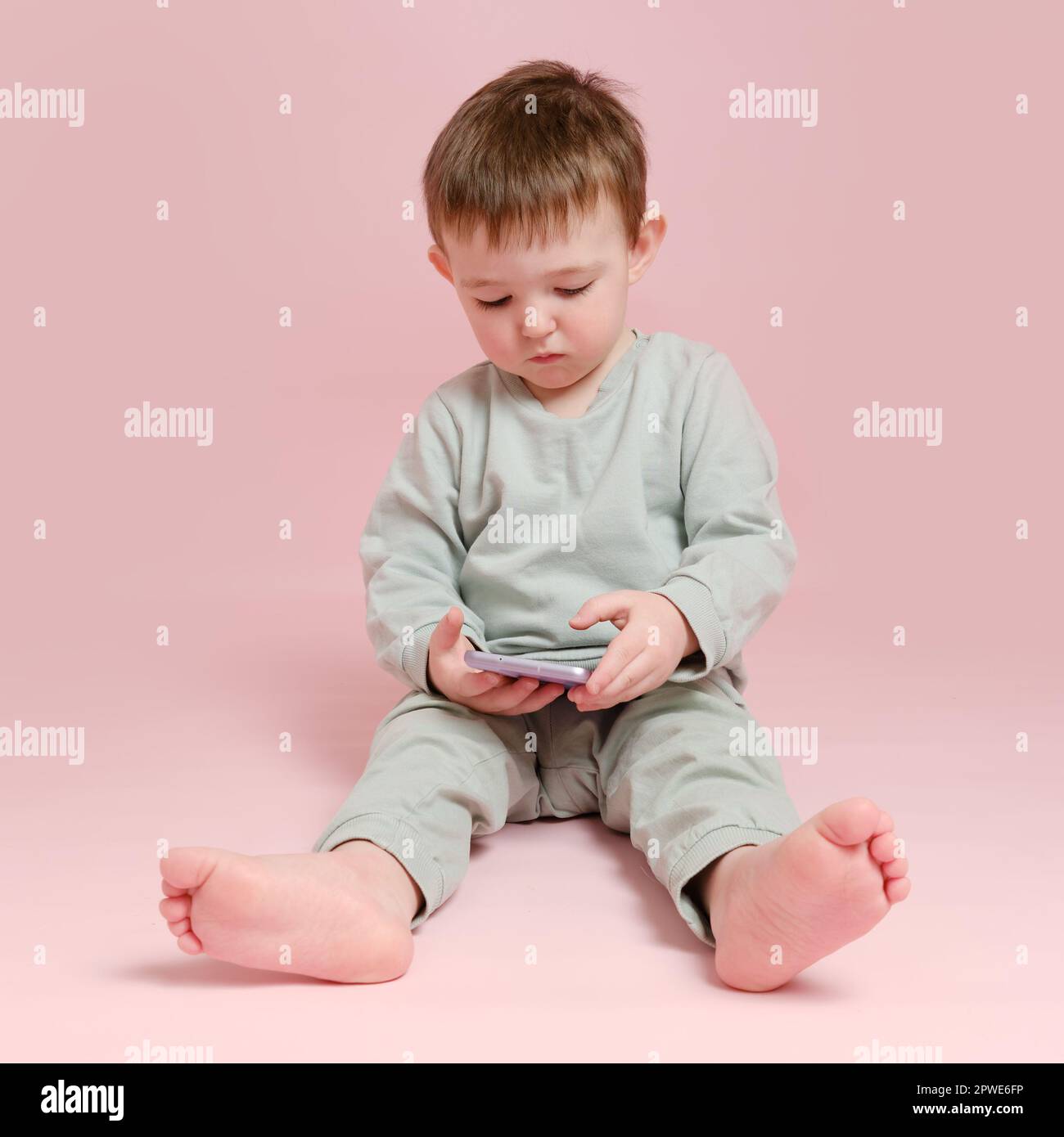 Happy toddler baby with mobile phone on studio pink background. Child ...