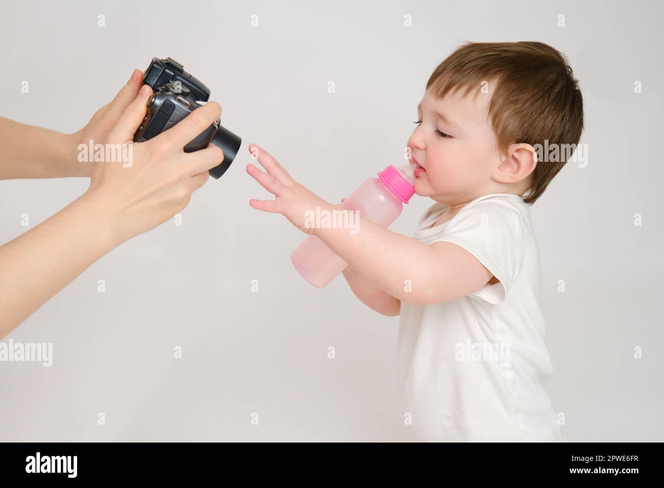 Woman mother photographs baby on photo camera, studio white background ...
