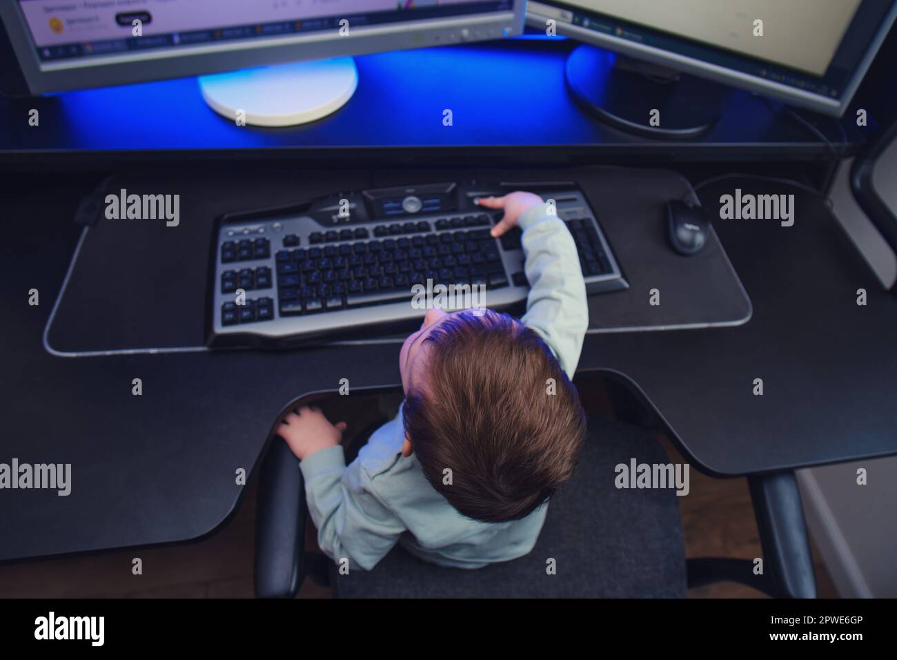 Happy baby is sitting at the computer keyboard next to the monitors. A ...