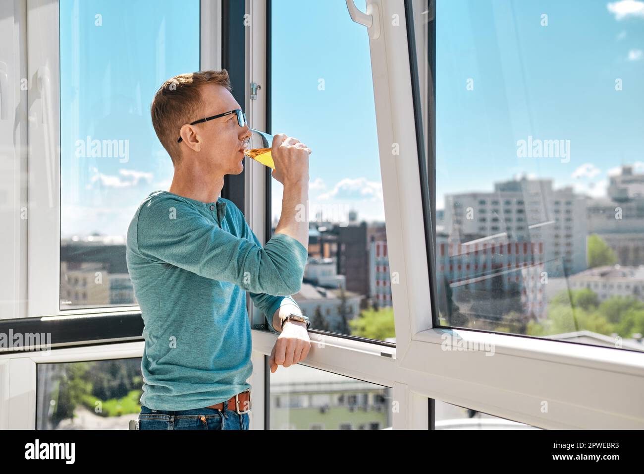 Middle aged man stands on balcony of high-rise building leaning against ...