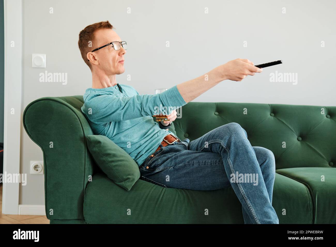 Man pointing tv remote control sitting on sofa in living room Stock ...