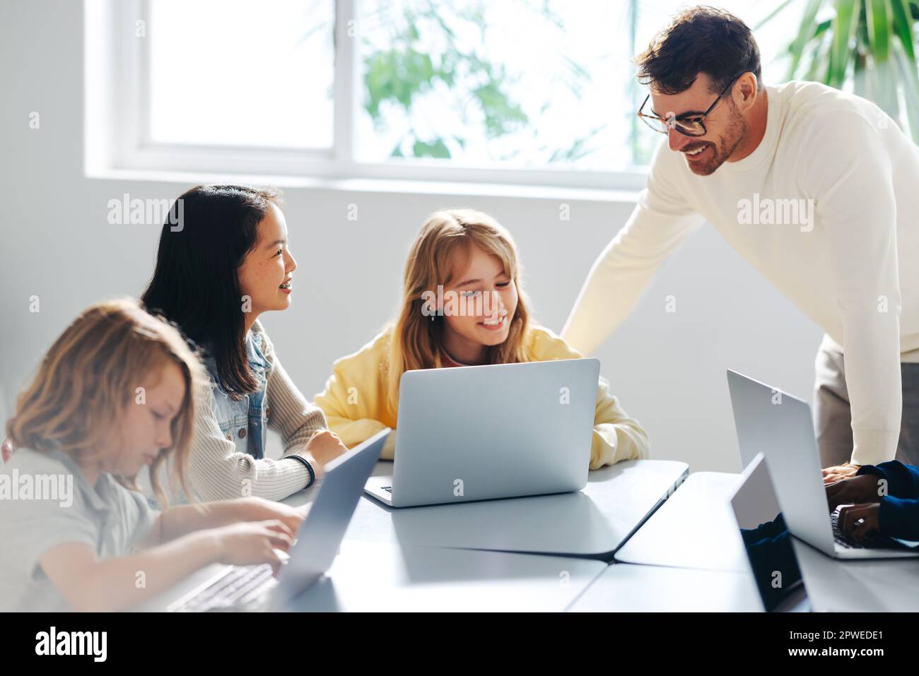 Computer science educator guiding a group of young students in a coding class. Teacher engaging ...