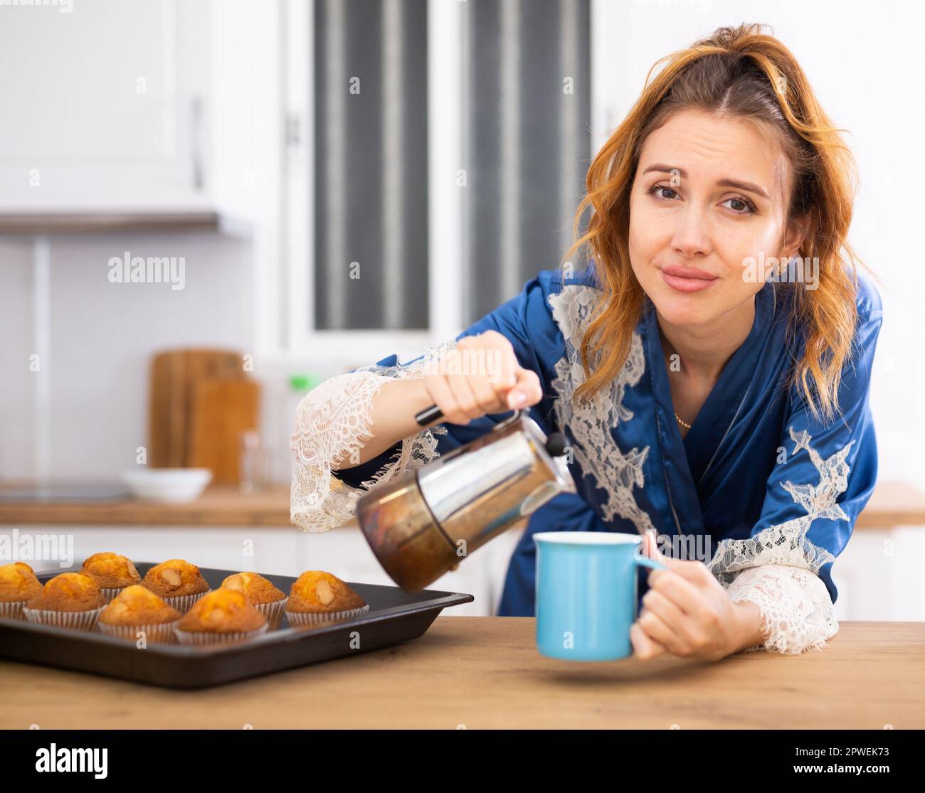 Upset just woken up woman in blue peignoir preparing coffee in kitchen Stock Photo - Alamy