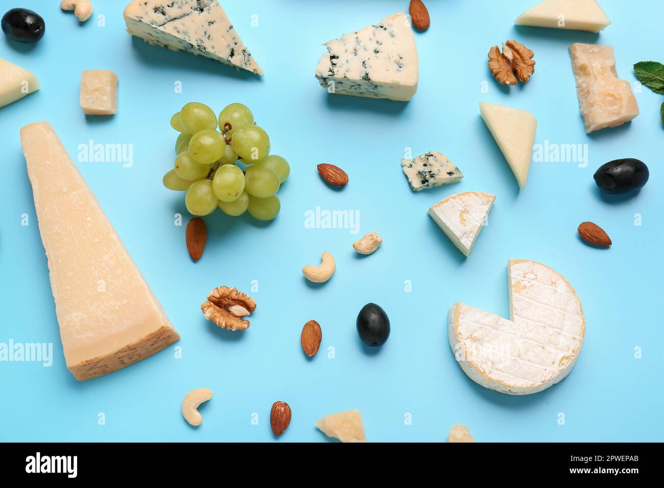 Different types of tasty cheese, nuts and grapes on blue background ...
