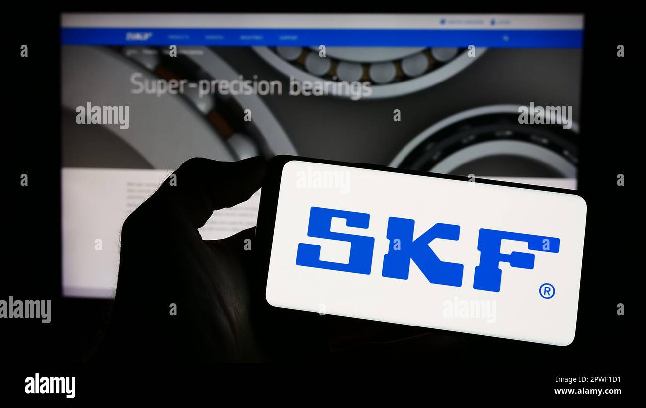 Person holding cellphone with logo of Swedish bearing manufacturing company SKF AB on screen in ...
