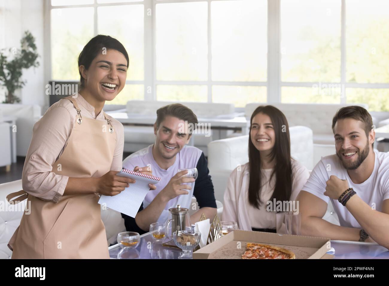 Indian waitress laughing with restaurant guests, group of young people ...