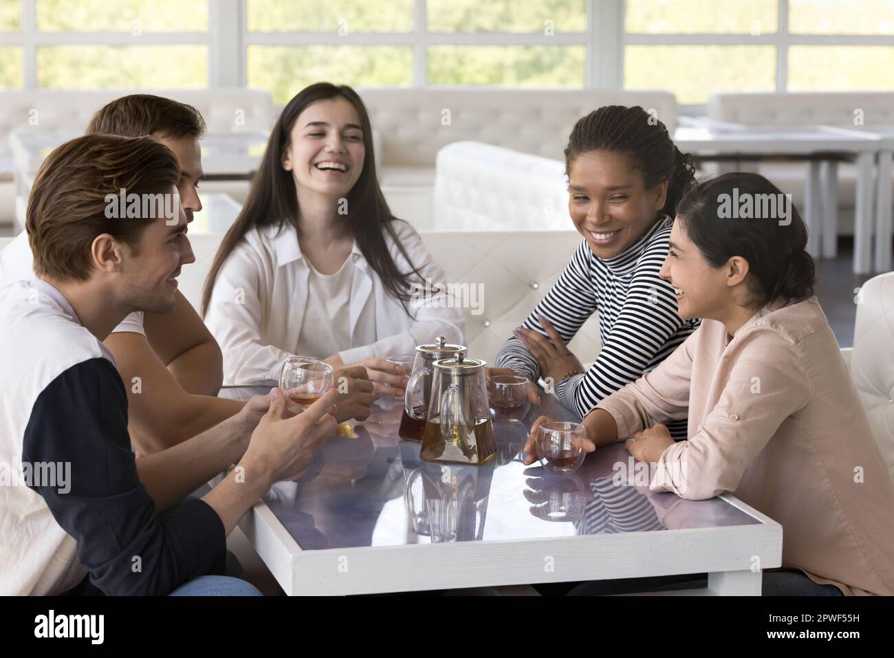 Friends talking while drinking tea seated at table in cafeteria Stock ...