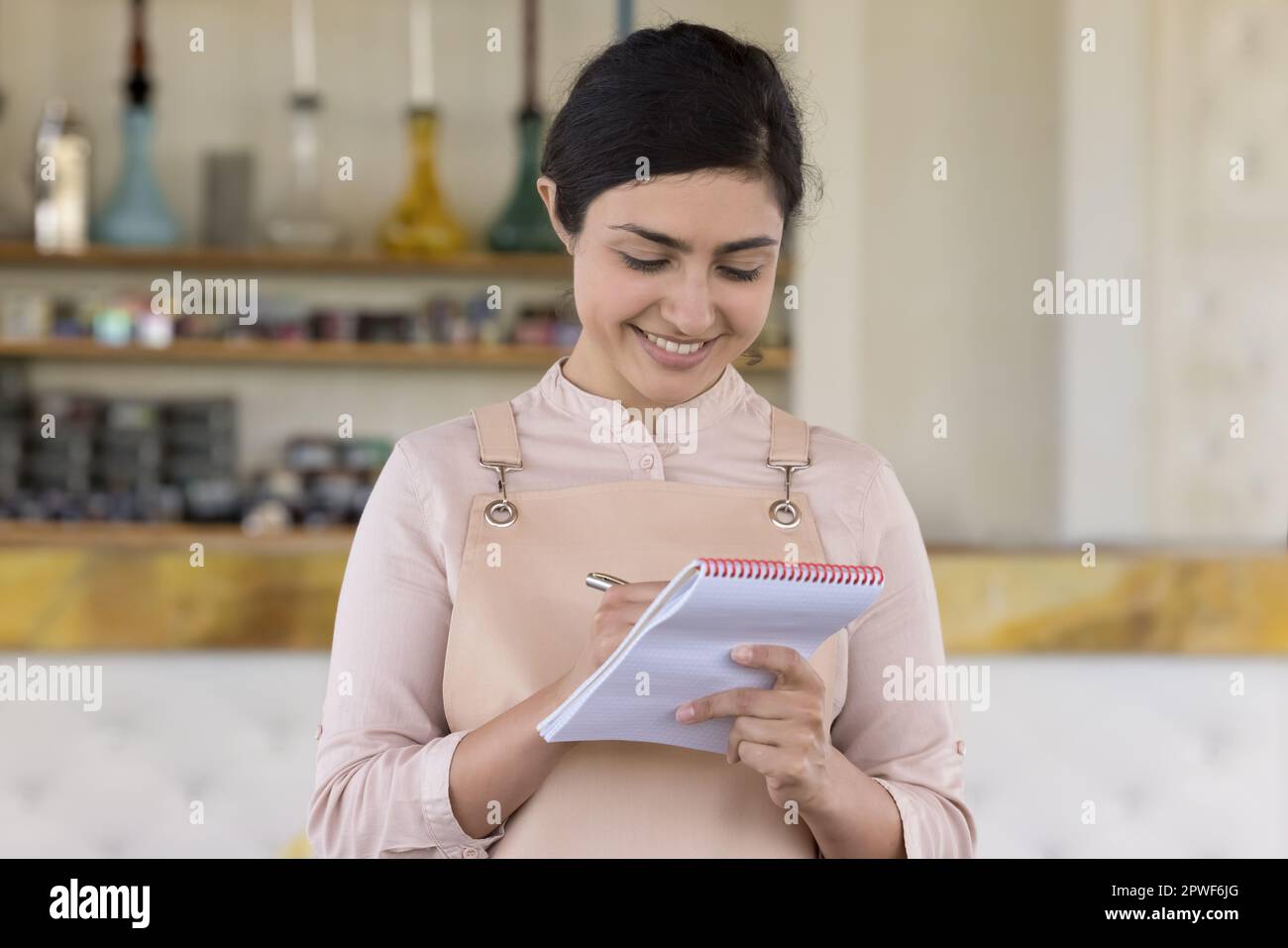 Pretty Indian waitress writing in notepad standing at workplace Stock ...