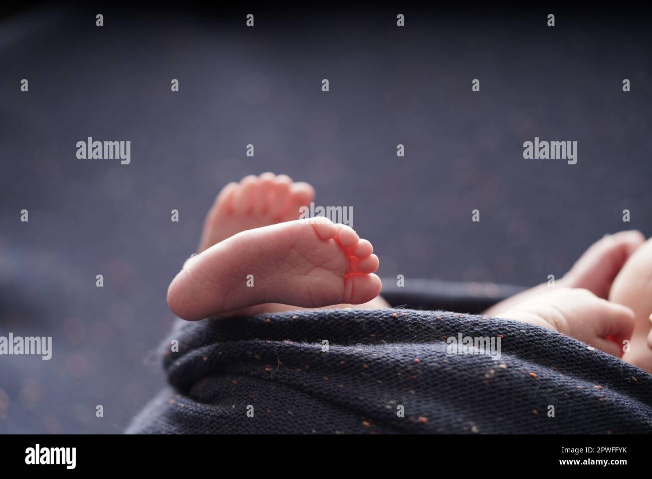 Tiny baby barefoot crossed on a navy blue background blanket. close-up ...