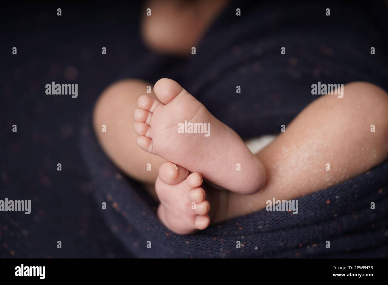 Tiny baby barefoot crossed on a navy blue background blanket. close-up ...