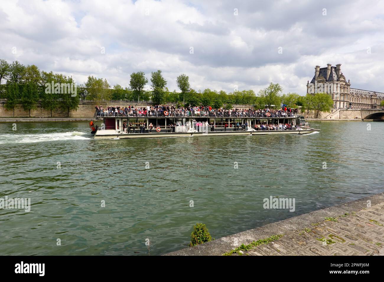 Tourist boat on Seine River, loaded with tourists, passing the Louvre ...