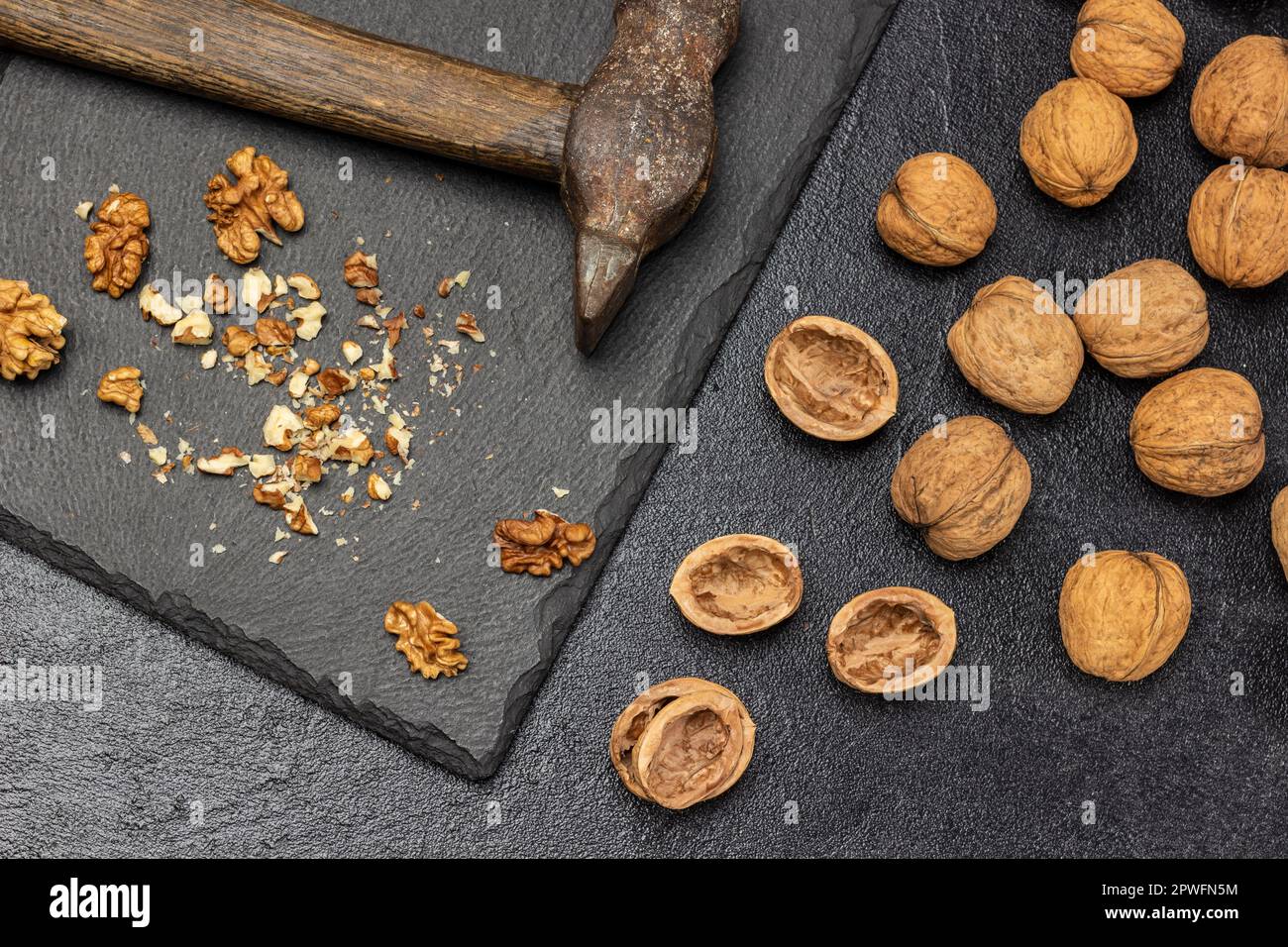 Crushed walnuts and a rusty old hammer on stone board. Nut shell and ...