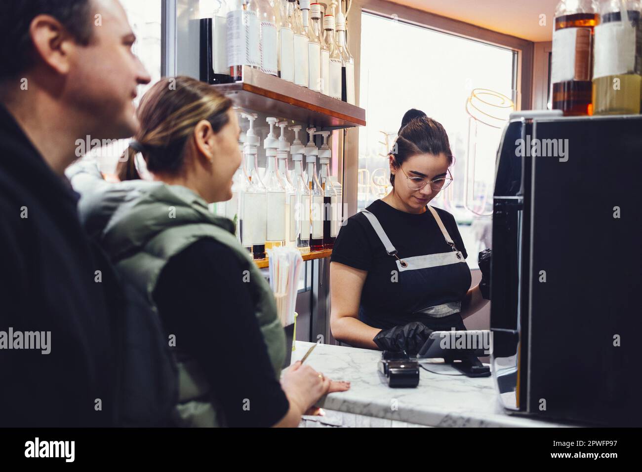 Young female barista takes order from her customers and selects coffee ...