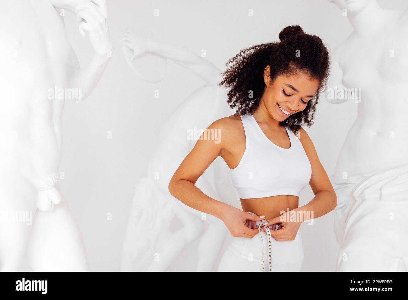 Slender attractive african woman in white sportswear measuring waist ...