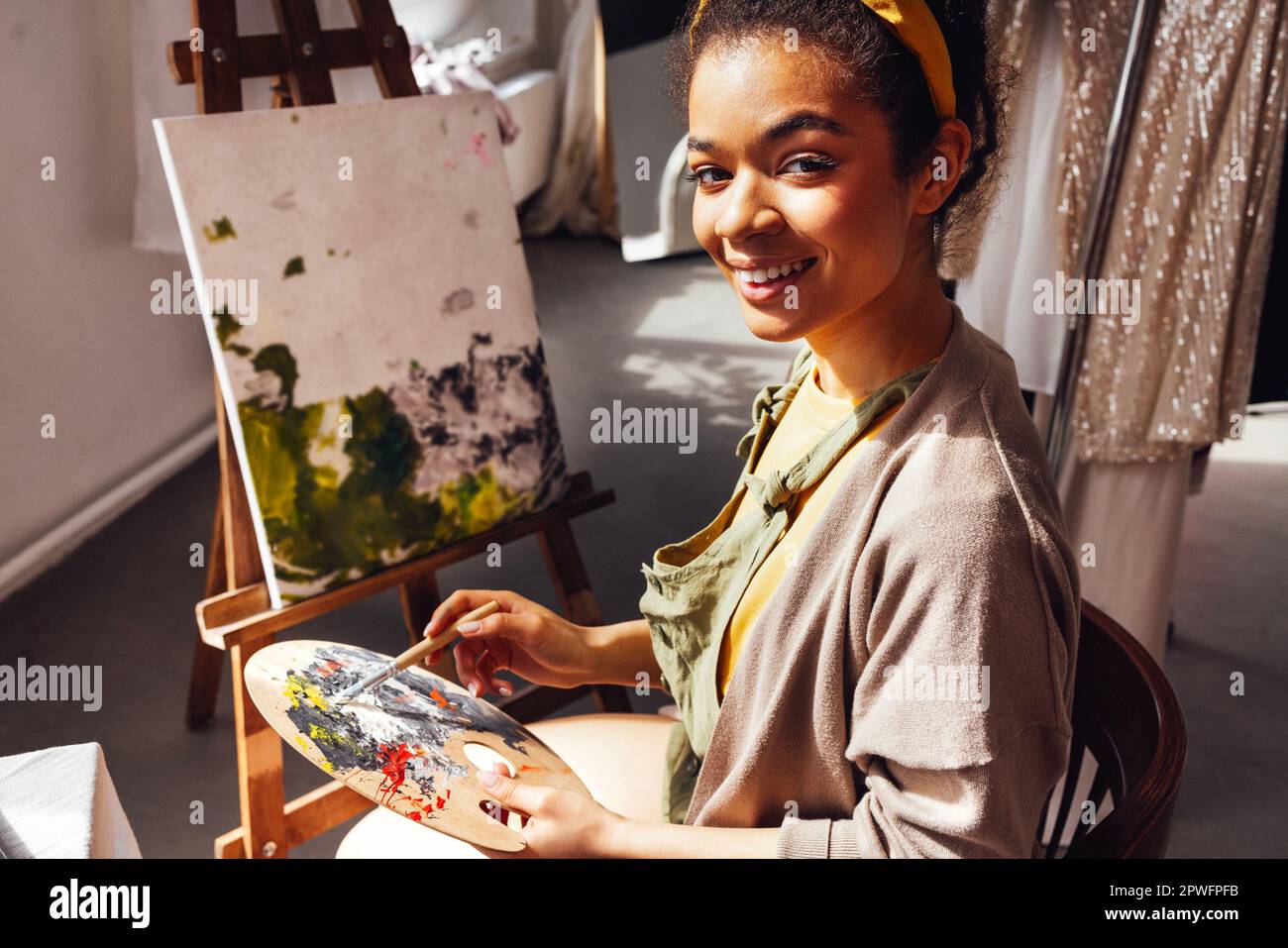 Young female creative pretty african american artist paints picture with oil paints in art ...