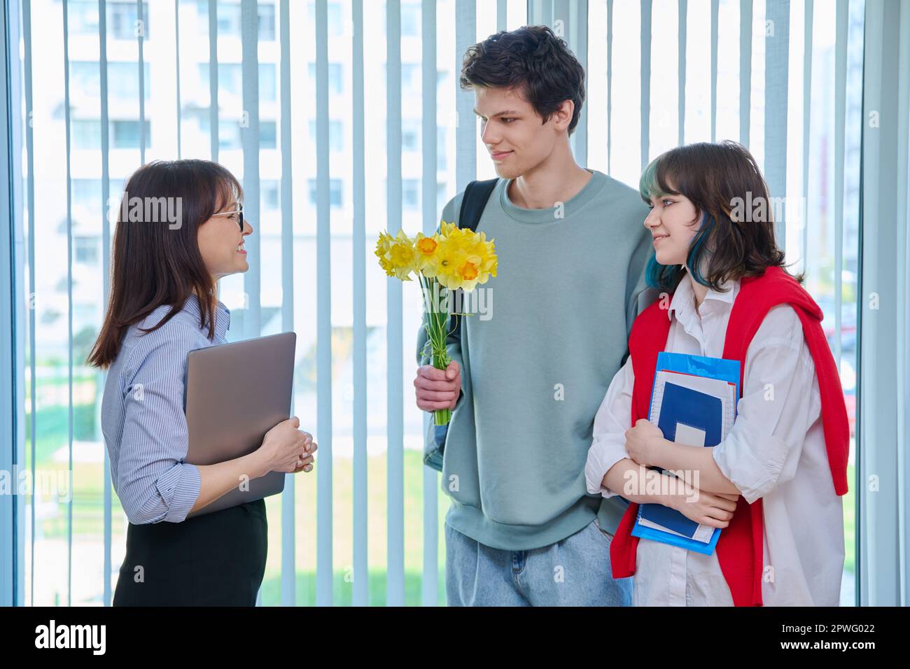 Teenage students congratulating female teacher with bouquet of flowers ...