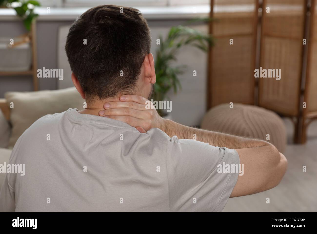 Man suffering from neck pain in living room, back view Stock Photo - Alamy
