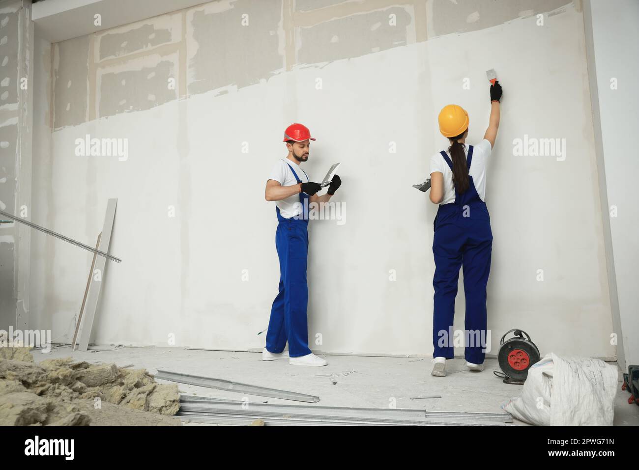 Professional workers plastering wall with putty knives in hard hats ...