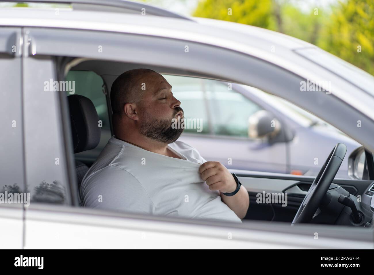 Exhausted overweight man driver feels blood pressure sitting inside car ...