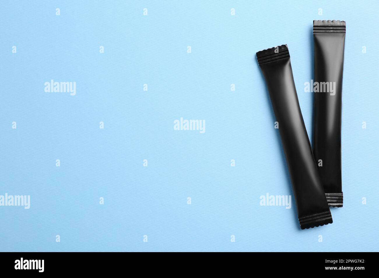 Black sticks of sugar on light blue background, flat lay. Space for ...