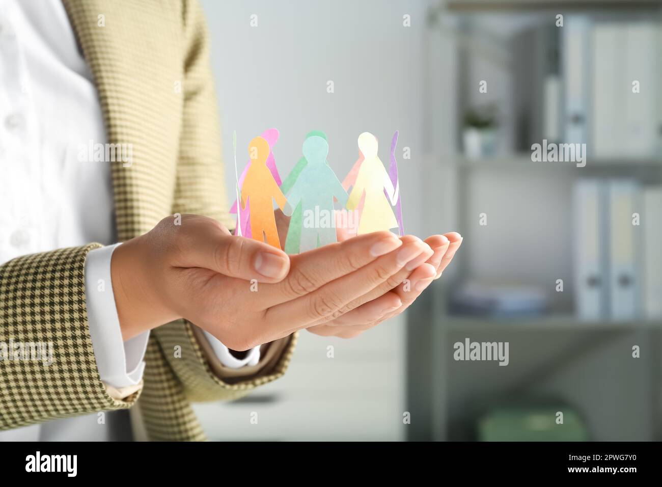 Woman holding paper human figures on blurred background, closeup ...