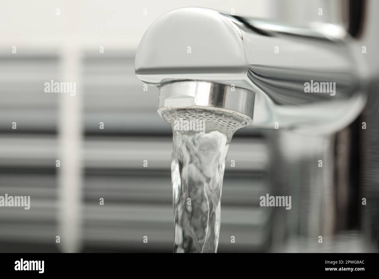Water flowing from tap on blurred background, closeup. Space for text ...