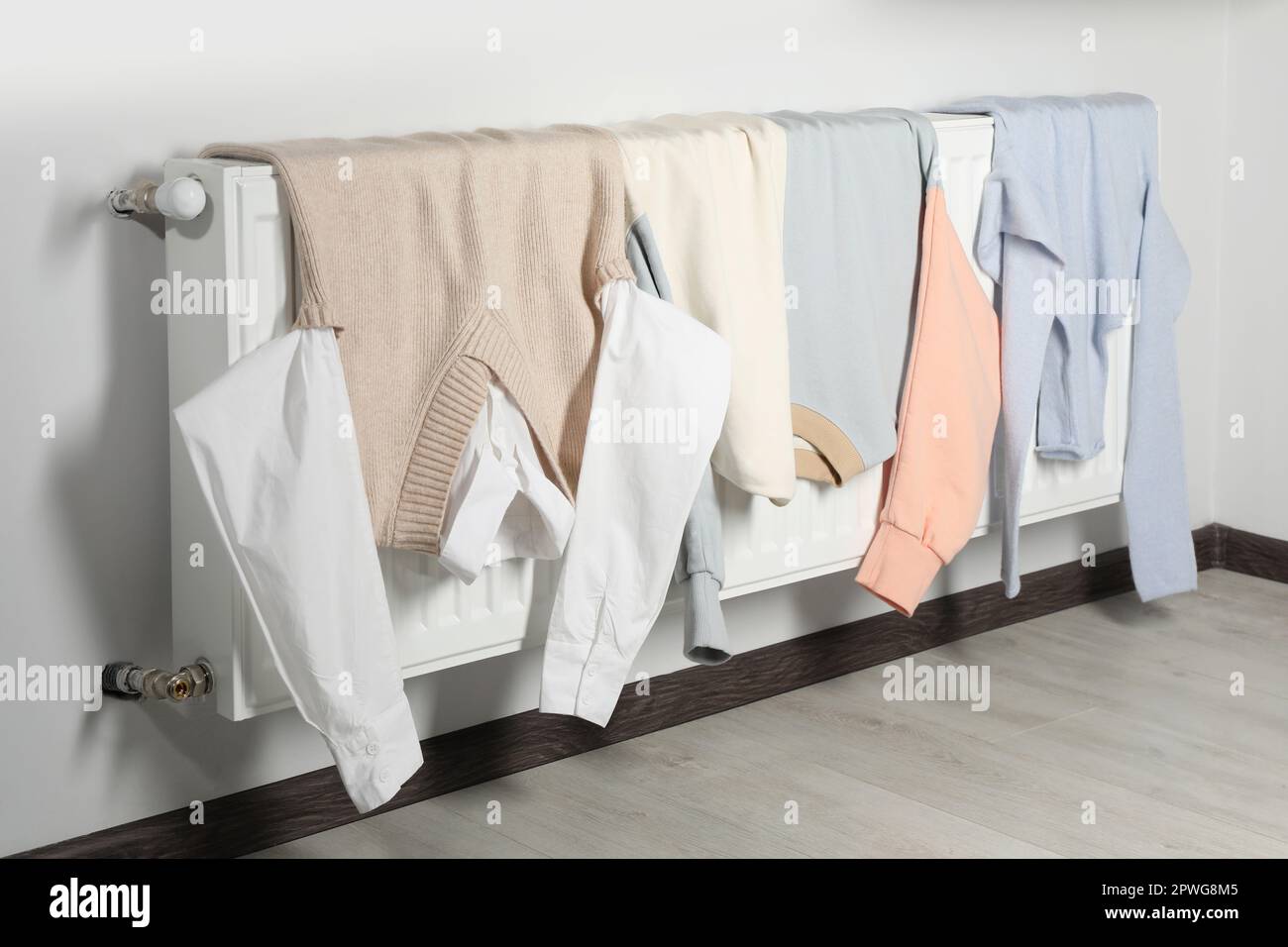 Clean clothes hanging on white radiator in room Stock Photo - Alamy