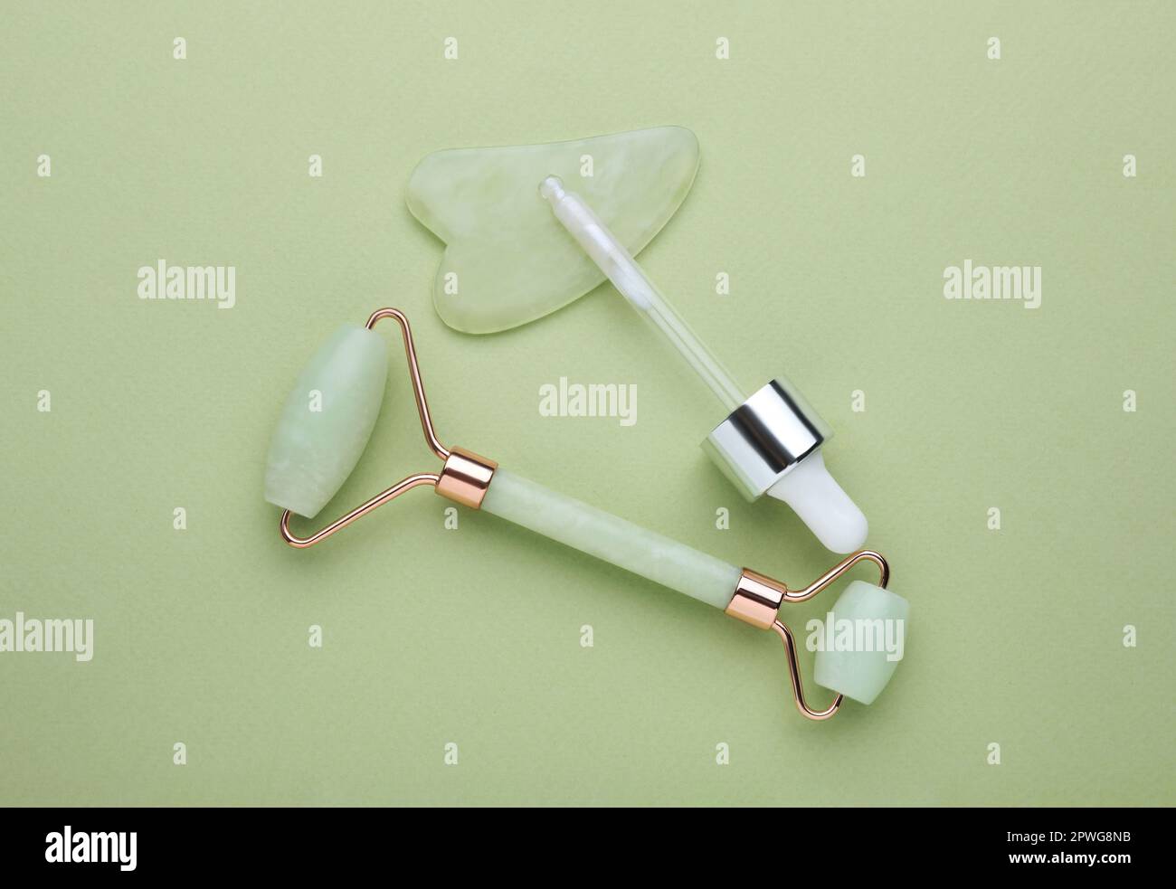 Jade gua sha tool, facial roller and dropper on light green background ...