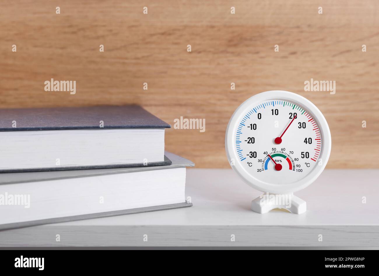 Round hygrometer with thermometer and books on white table Stock Photo ...