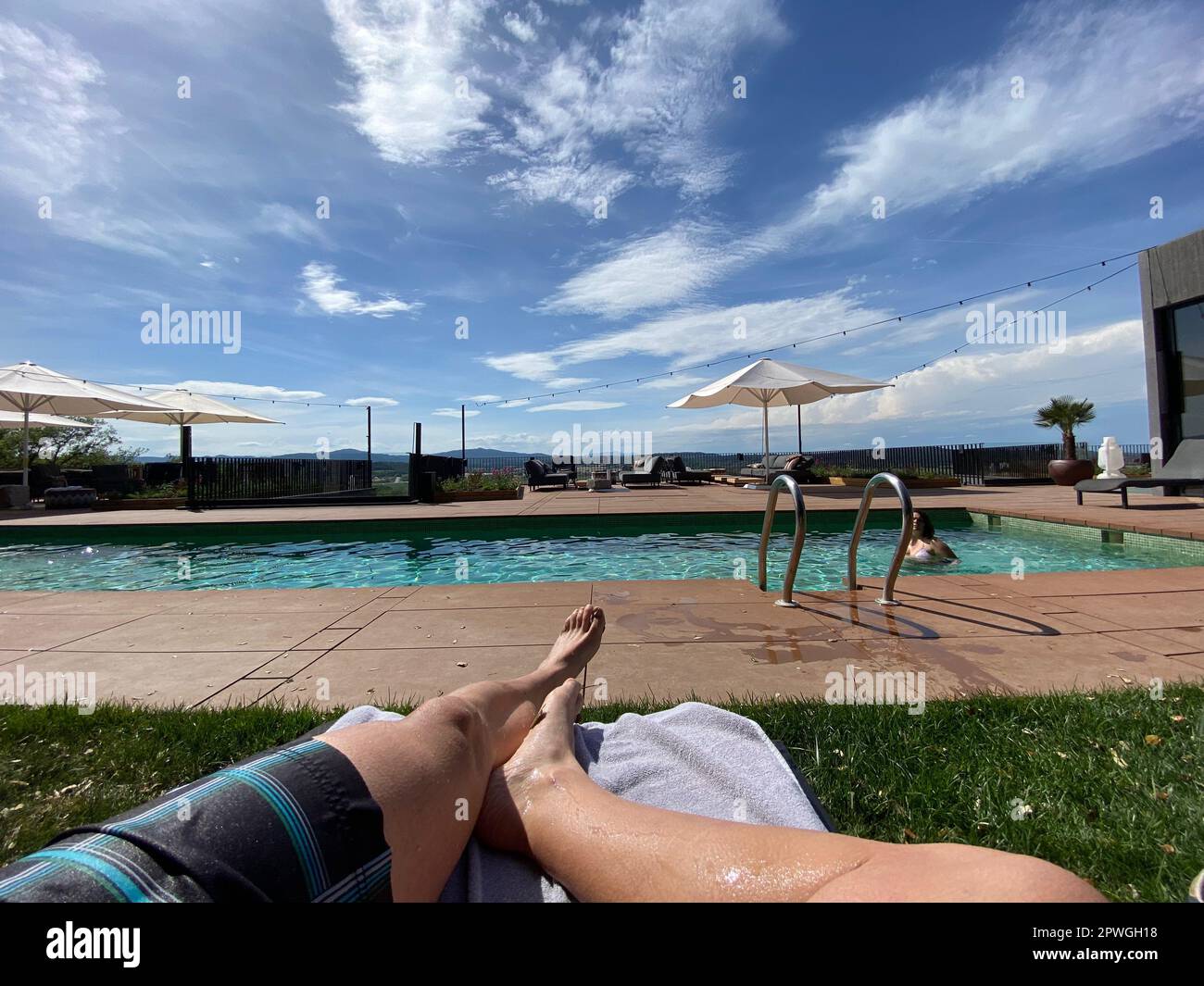Lying on a sun lounger with white legs in front of an outdoor swimming ...