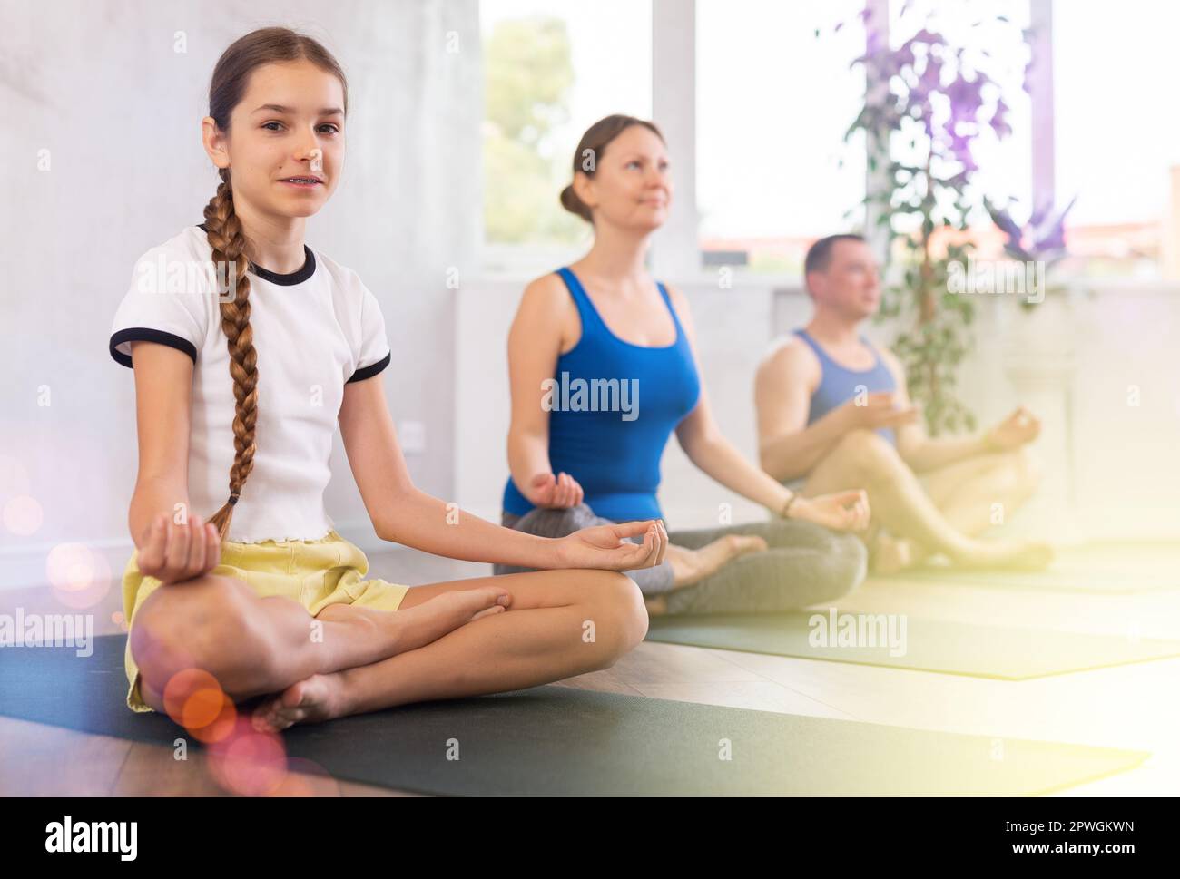 Pleasant preteen girl practicing lotus pose of yoga with her family ...