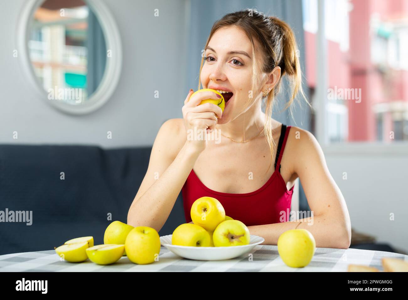 Positive woman sitting at table and biting green apple Stock Photo - Alamy