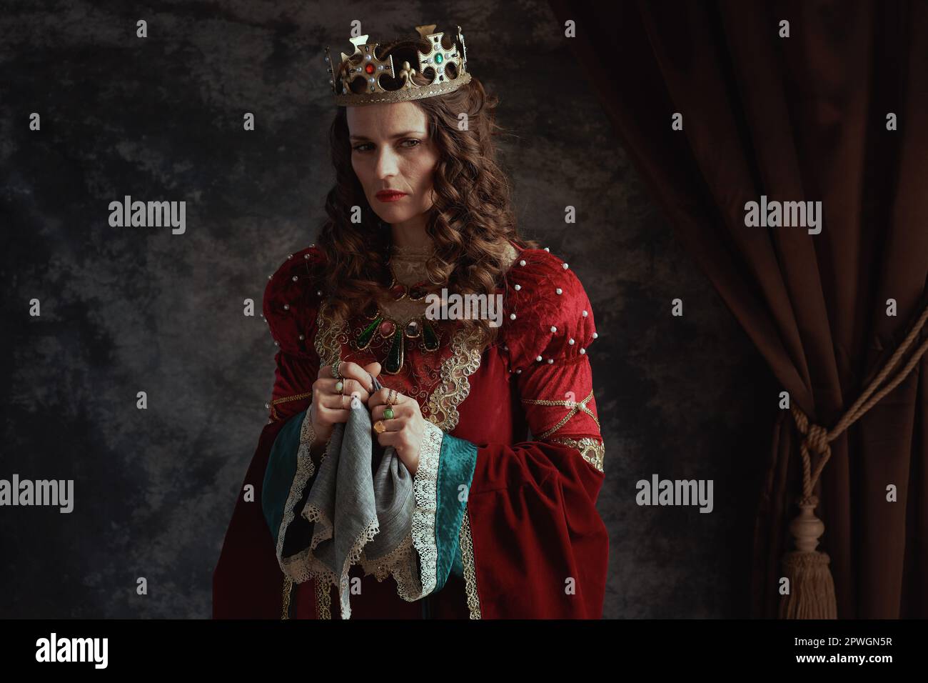 unhappy medieval queen in red dress with handkerchief and crown on dark ...